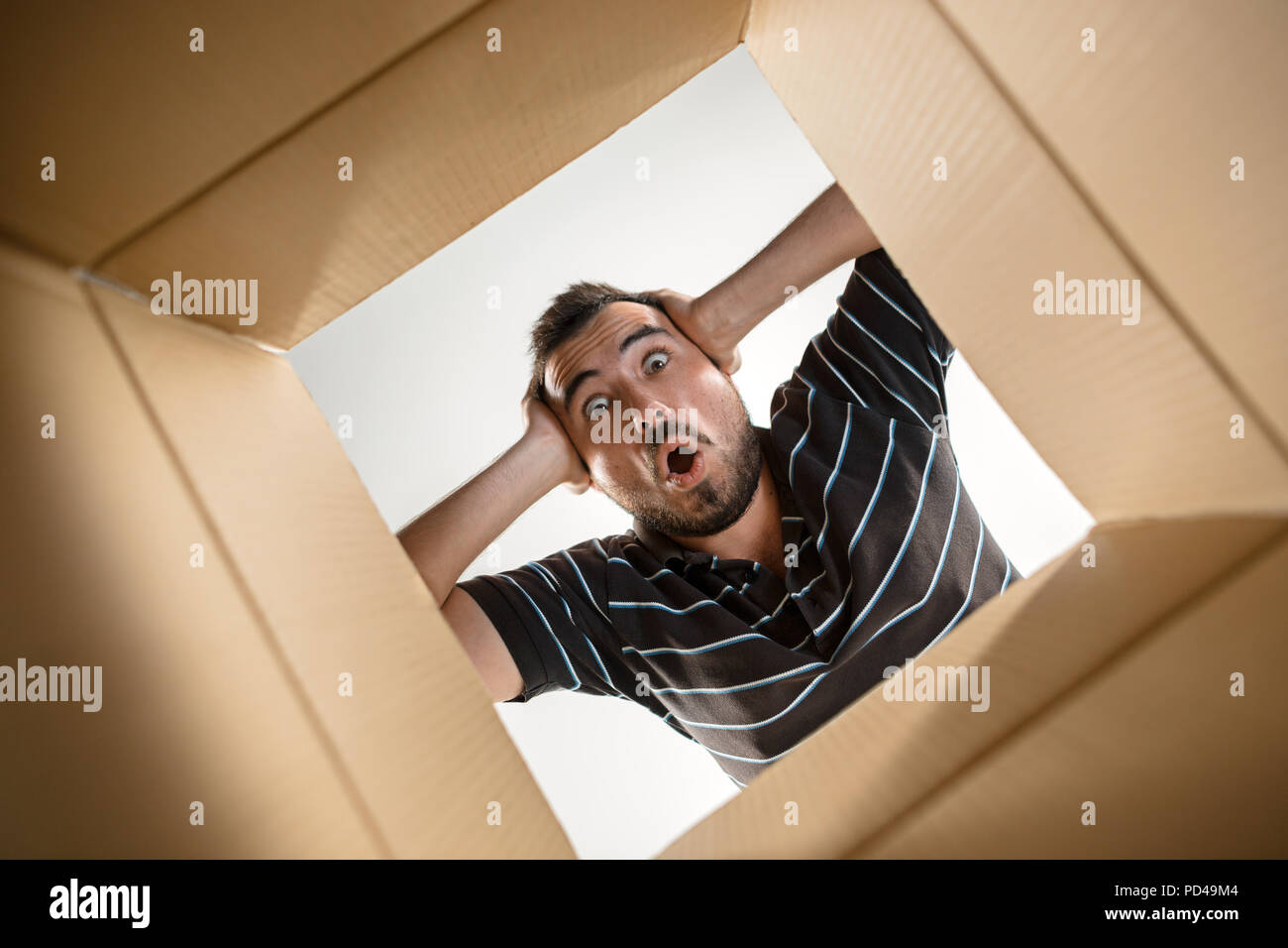 The surprised man unpacking, opening carton box and looking inside. The ...