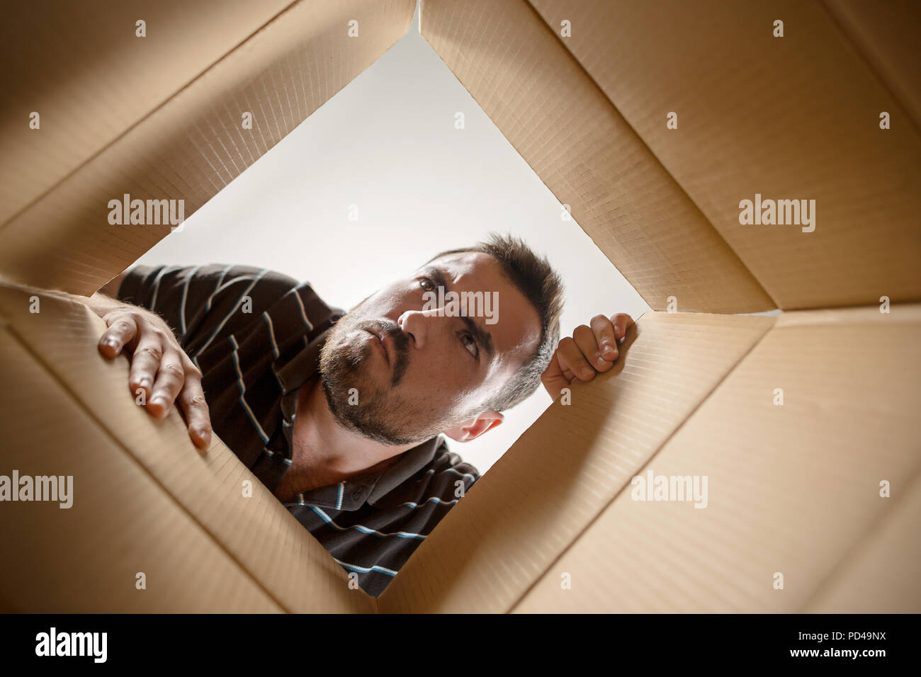 The surprised man unpacking, opening carton box and looking inside. The ...