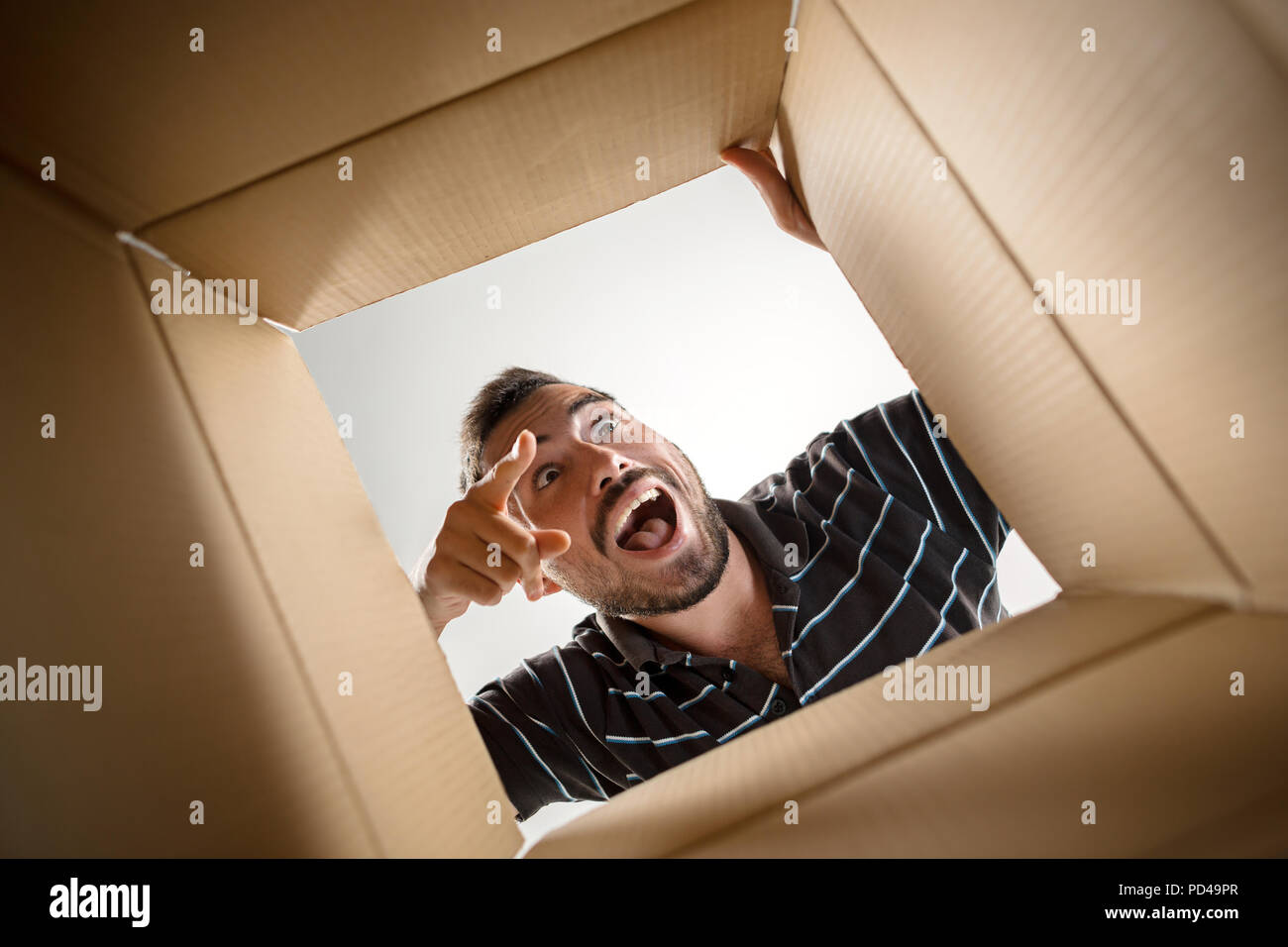 The surprised man unpacking, opening carton box and looking inside. The ...