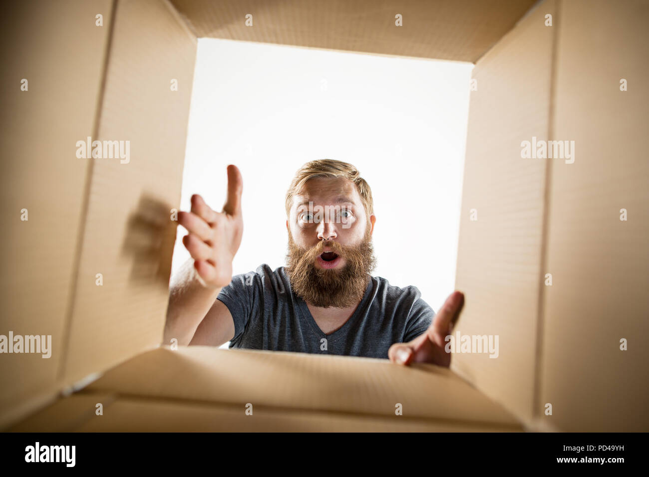 The surprised man unpacking, opening carton box and looking inside. The ...
