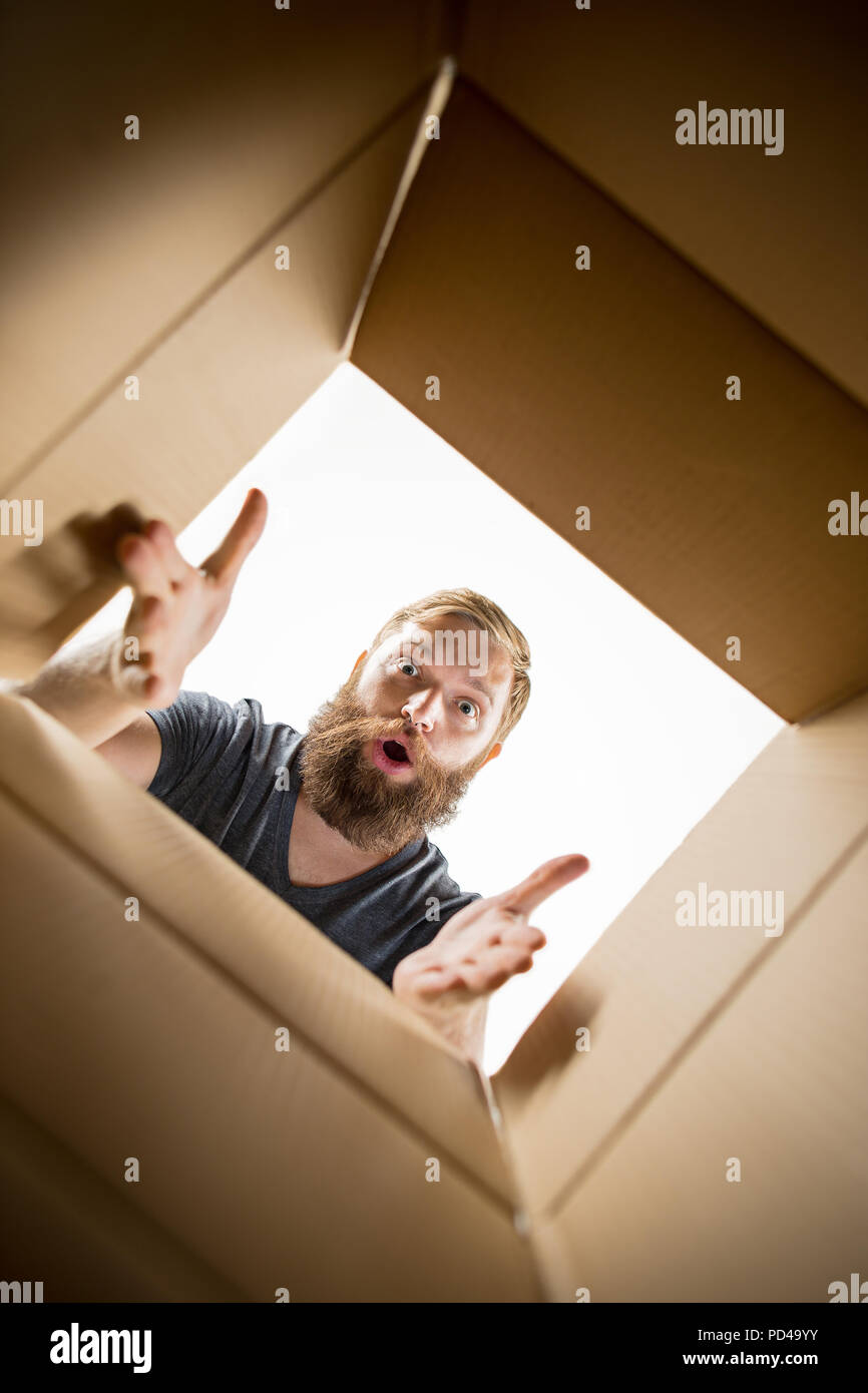 The surprised man unpacking, opening carton box and looking inside. The ...