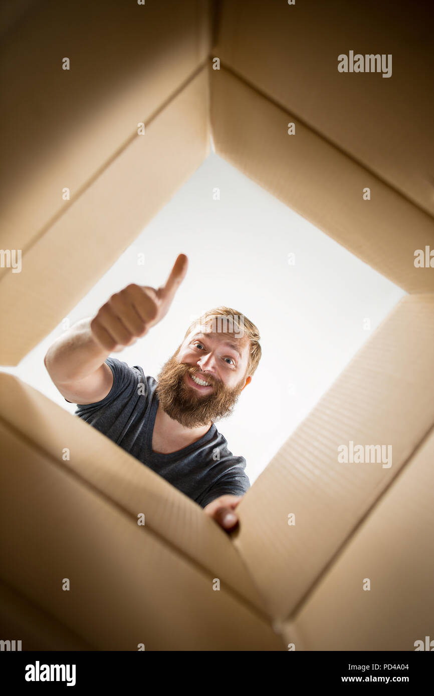 The surprised man unpacking, opening carton box and looking inside. The ...