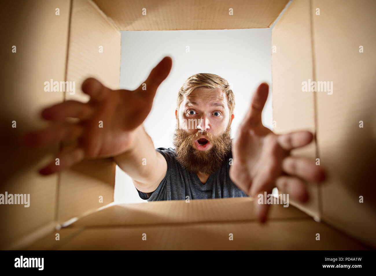 The surprised man unpacking, opening carton box and looking inside. The ...