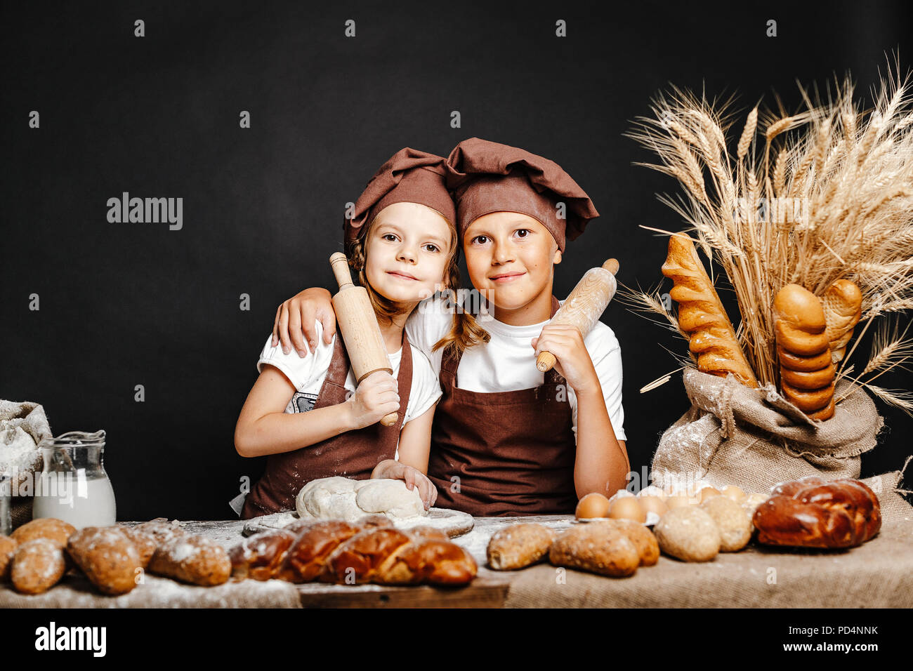 Adorable girl with brother in chief hats and aprons cooking at table ...