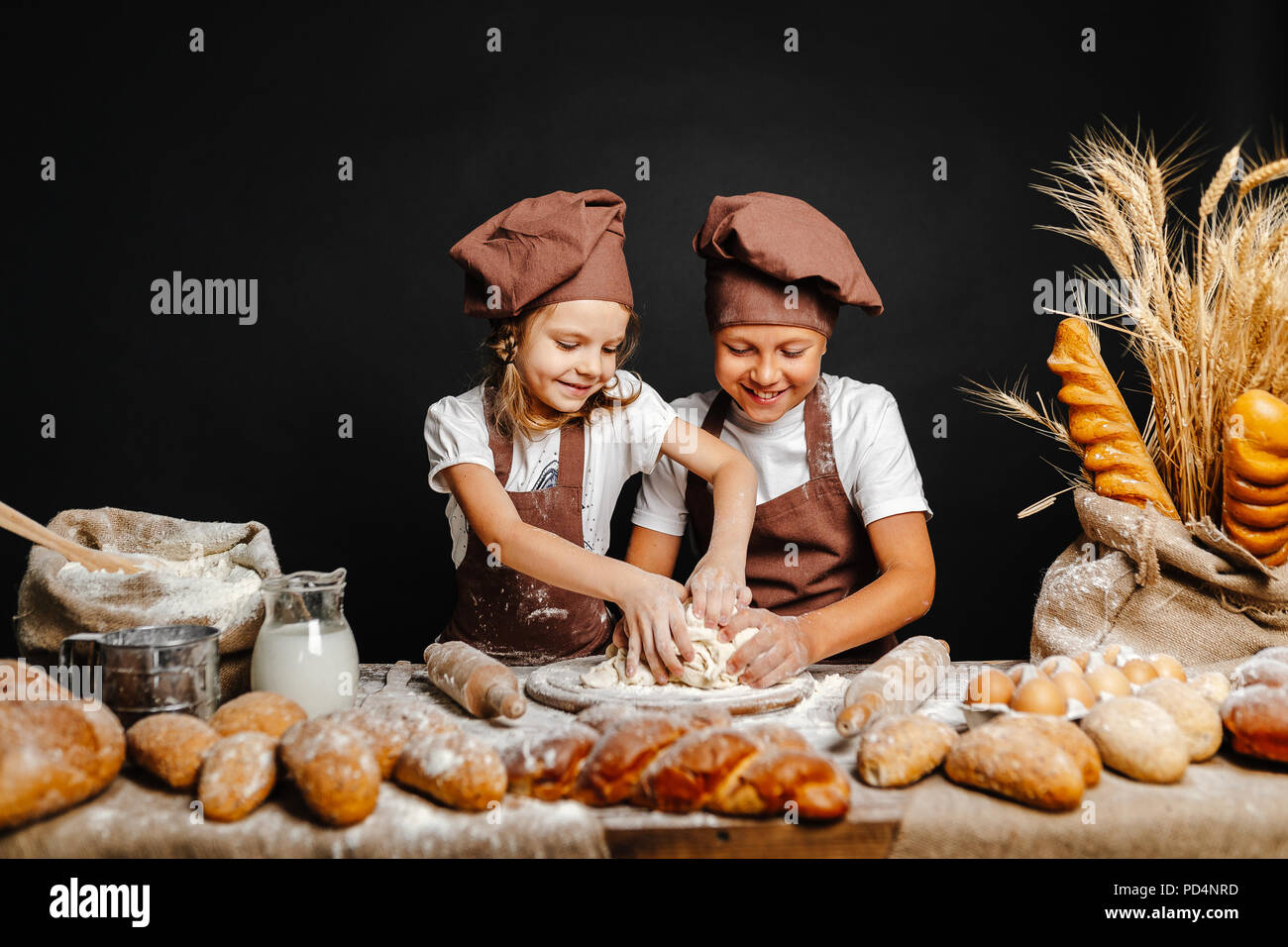 Adorable girl with brother in chief hats and aprons cooking at table ...