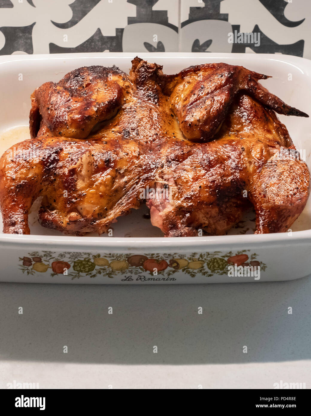 Grilled spatchcock chicken, in a serving dish on a white quartz kitchen ...