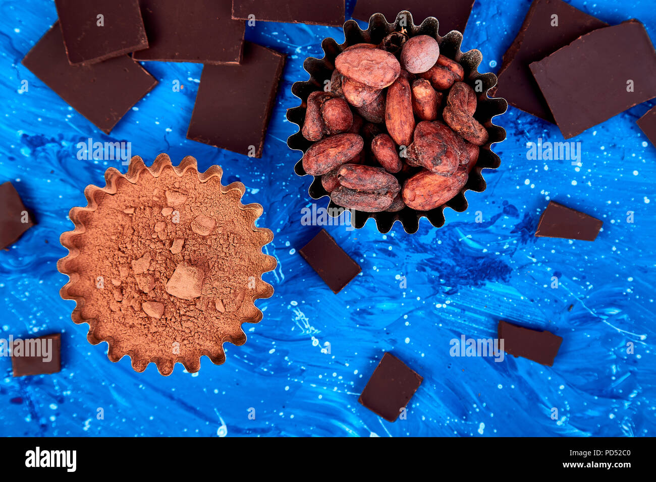Cocoa beans background on blue table. Dark chocolate pieces and crushed ...