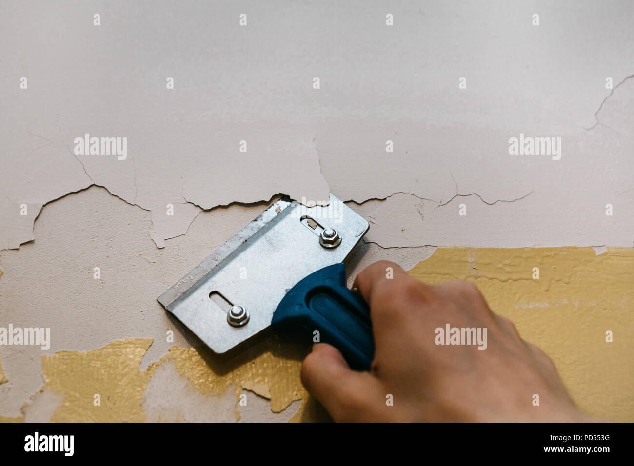 Close-up. A man with a scraper removes the old covering from the wall ...