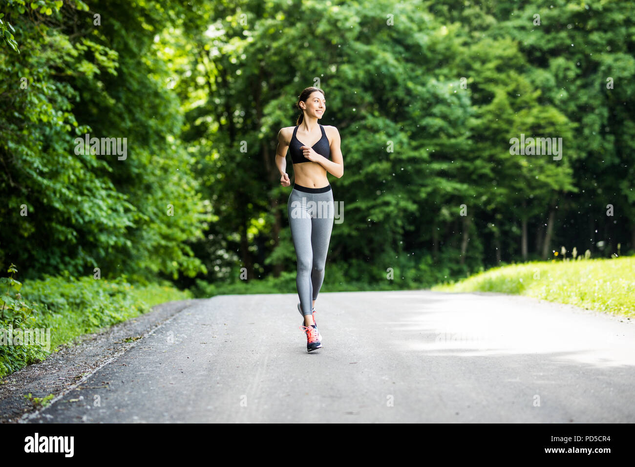Young lady running. Woman runner running through the spring park road ...