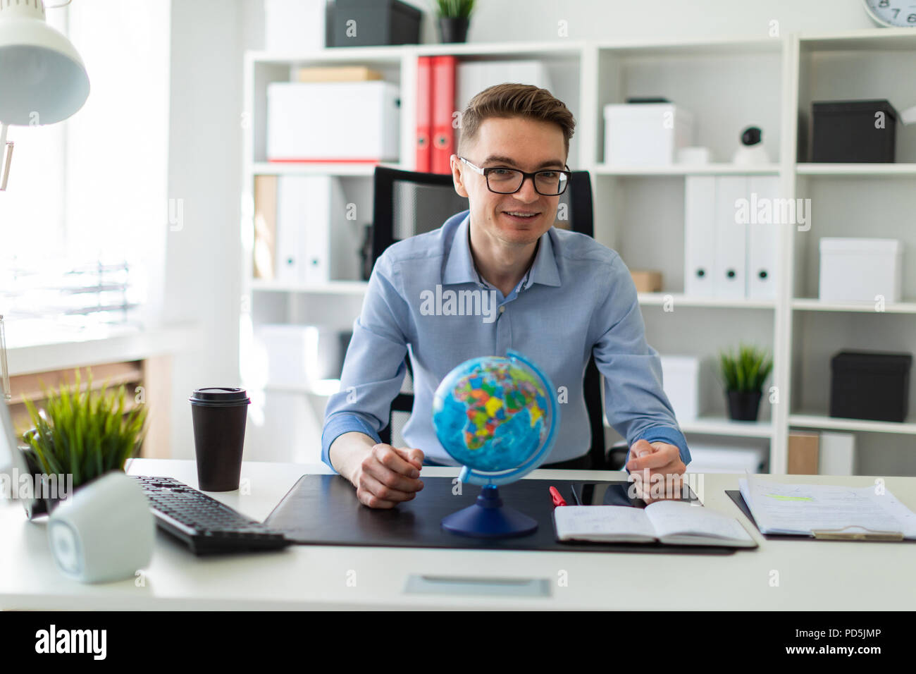 A young man sits in the office at a computer desk and in front of him ...