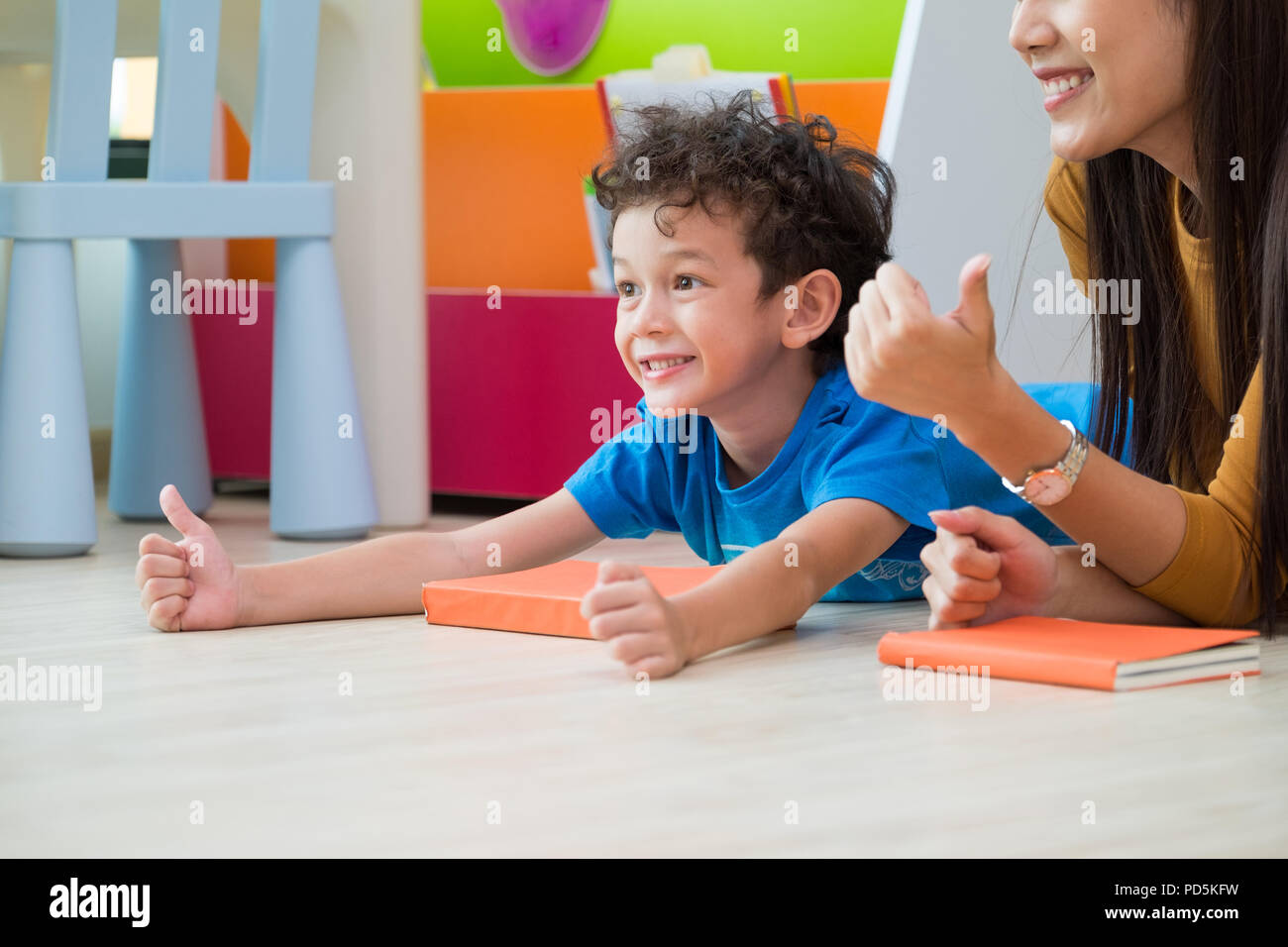 kid boy thumbs up with teacher while lying down on classroom floor at ...