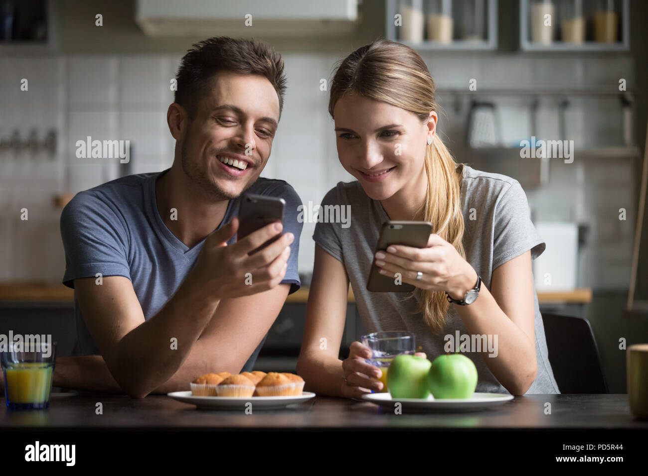 Smiling happy couple laughing using smartphones apps having brea Stock ...
