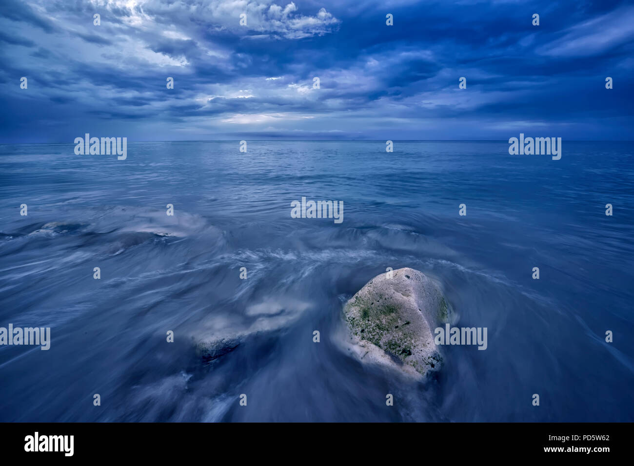 Blue hour by the sea with rocks in the foreground with water motion ...