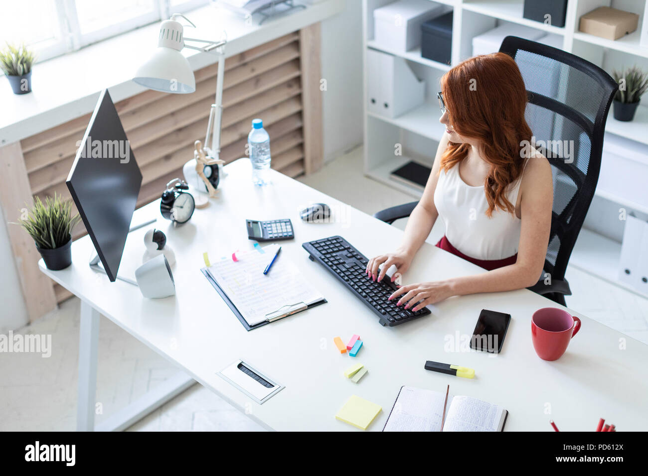 Beautiful young girl is sitting at the desk in the office and typing on ...