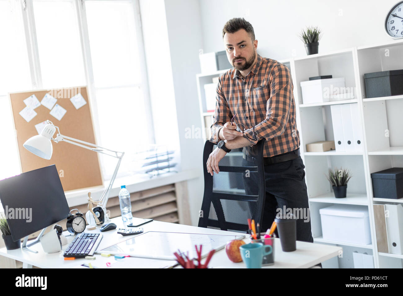 A man stands in the office near a computer desk and puts his hands on ...