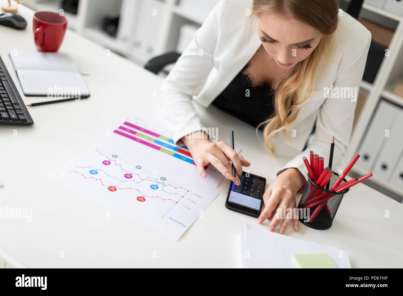 A young girl sits at a computer desk in the office and counts on a ...