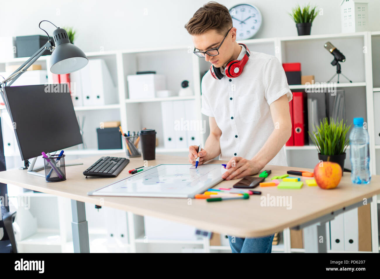 A young man in glasses stands near a computer desk. A young man draws a ...