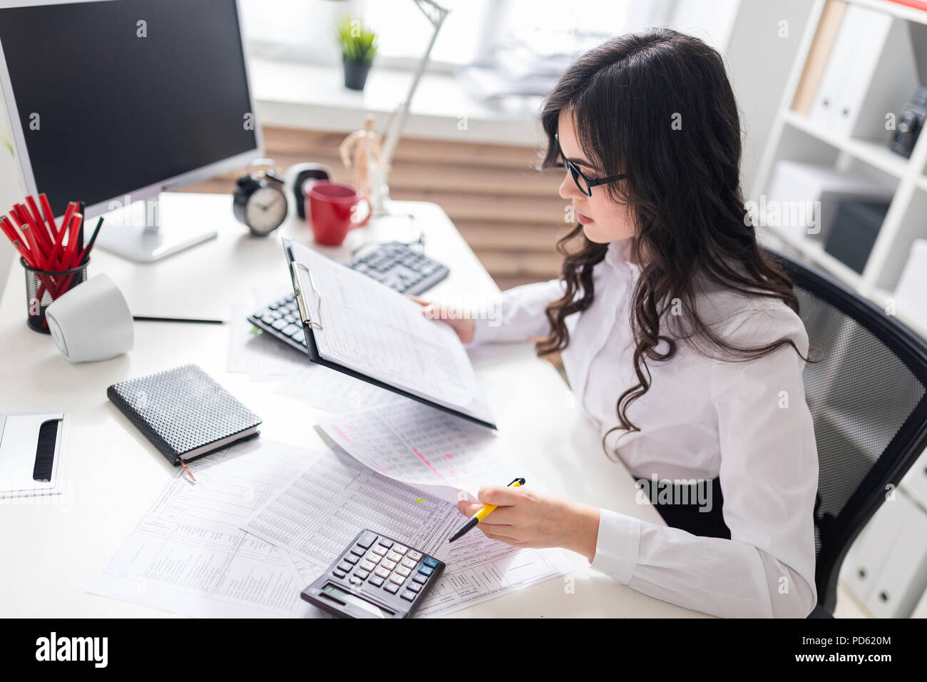 A young girl sits at the office desk and checks documents Stock Photo ...