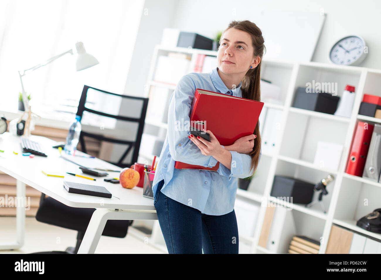 A young girl in the office is standing, leaning on a table, and is ...