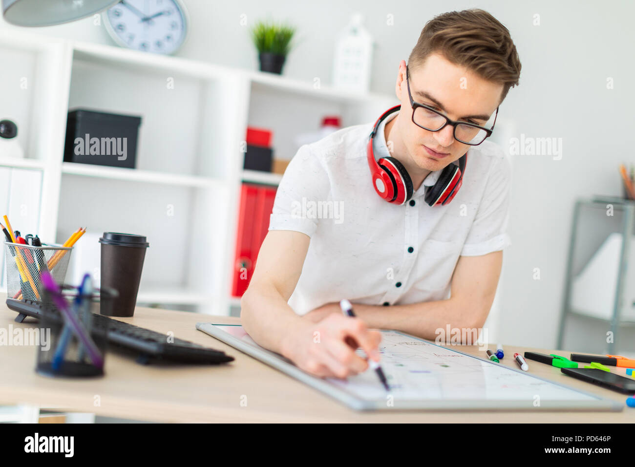 A young man in glasses stands near a computer desk. A young man draws a ...