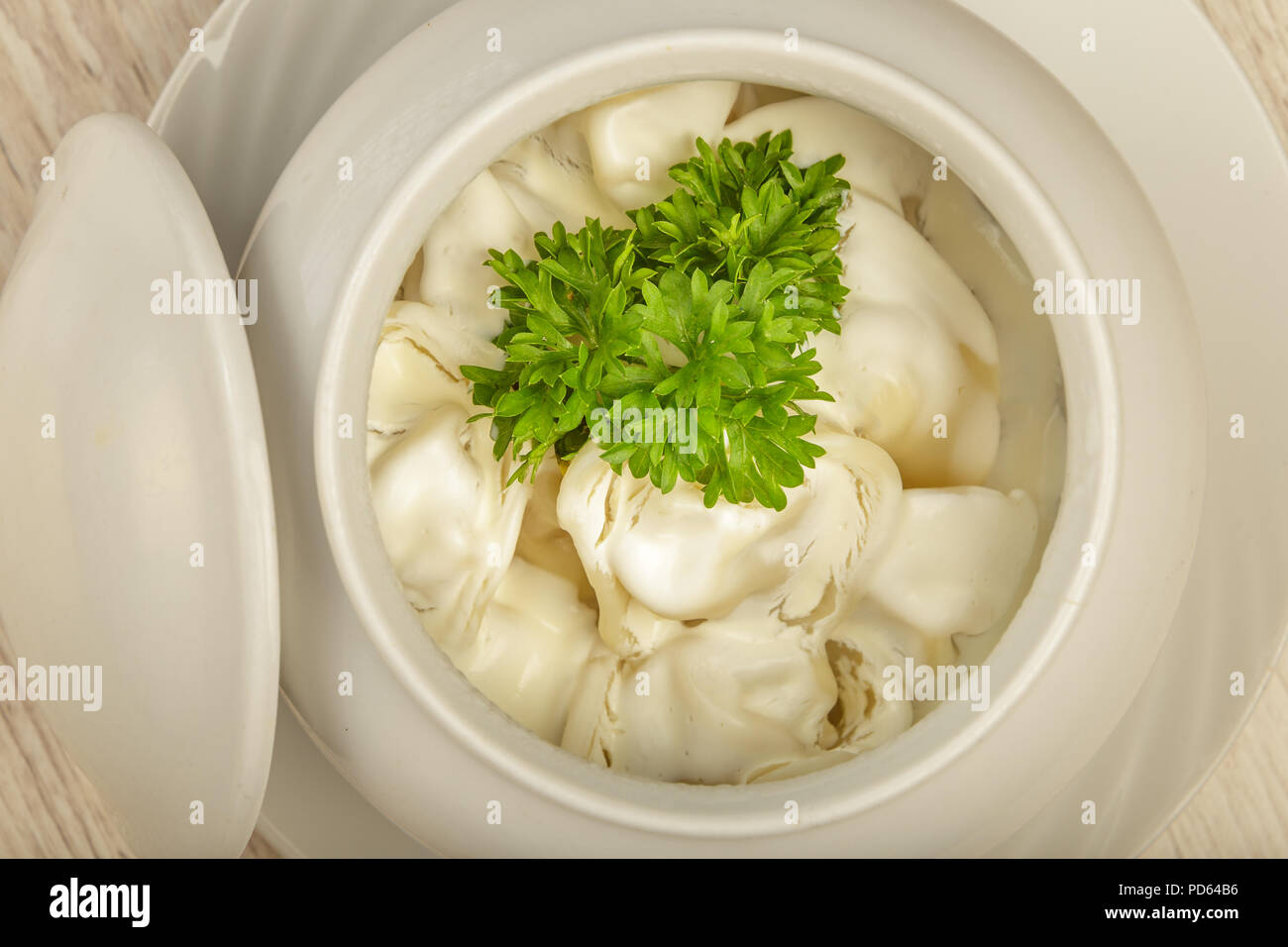 Dumplings in a white pot with sour cream and greens on a wooden ...