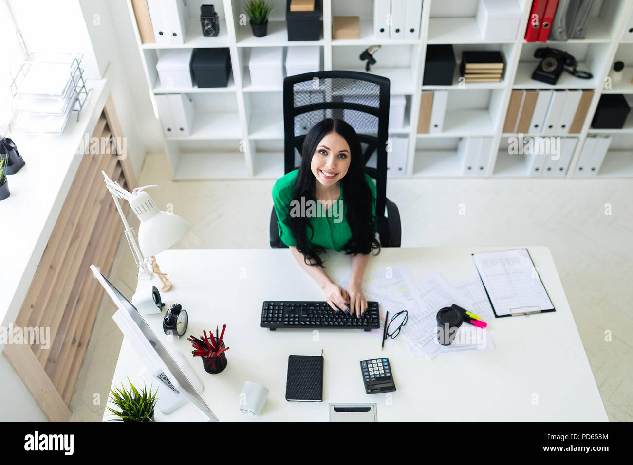 Top view of a young girl sitting at an office desk and typing on a ...