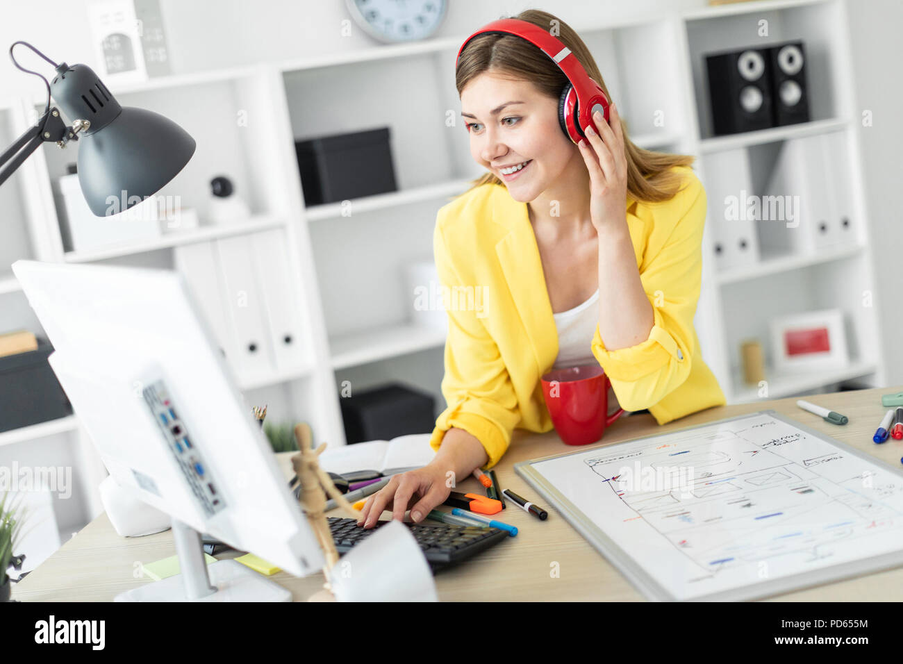 A young girl in headphones is working at the computer and is drinking ...