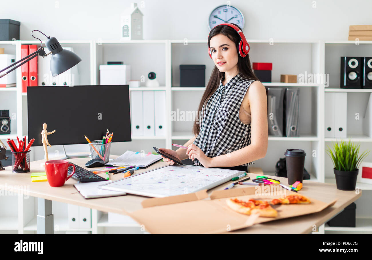 A young girl stands near a table and holds a marker and a telephone in ...