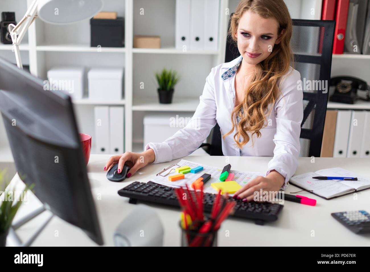 Beautiful young girl sitting at desk in office and working at computer ...