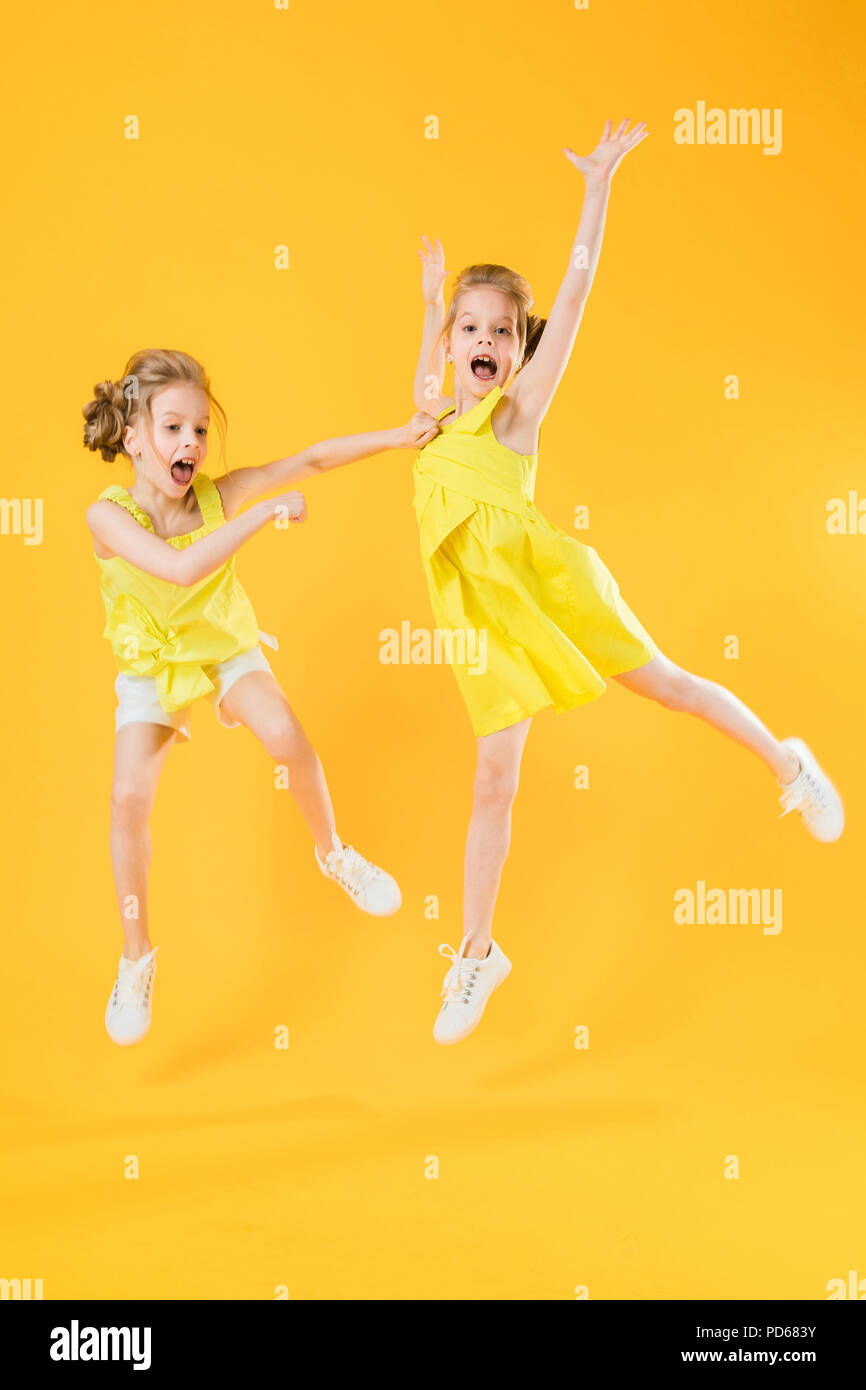 The girls of the twins are dancing together on a yellow background ...