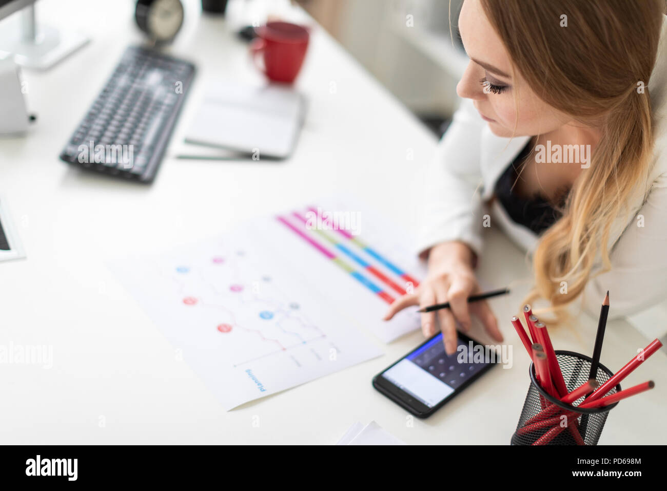 A young girl sits at a computer desk in the office and counts on a ...