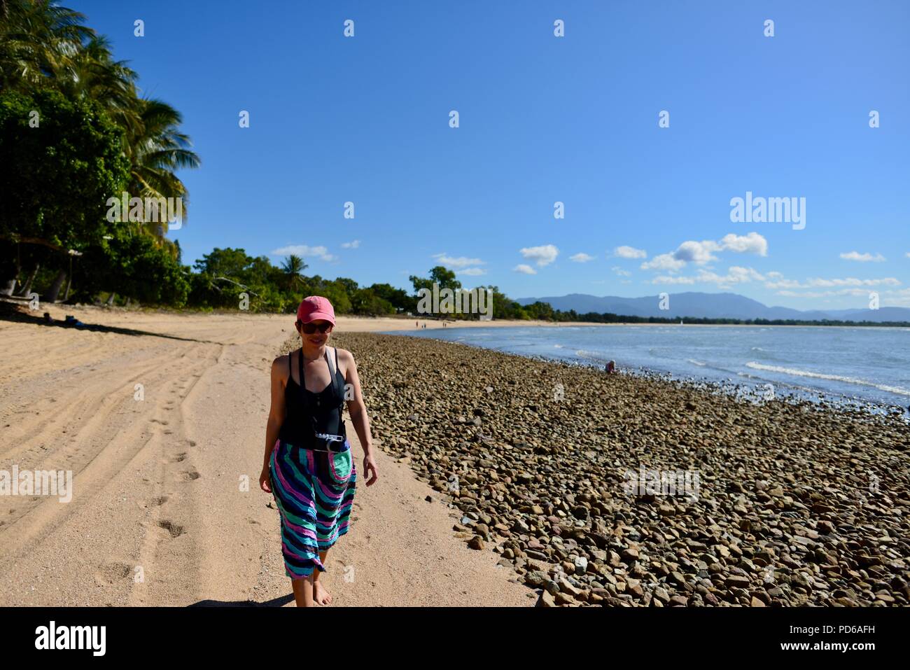 Woman walking along a sandy and rocky beach towards the hi-res stock ...