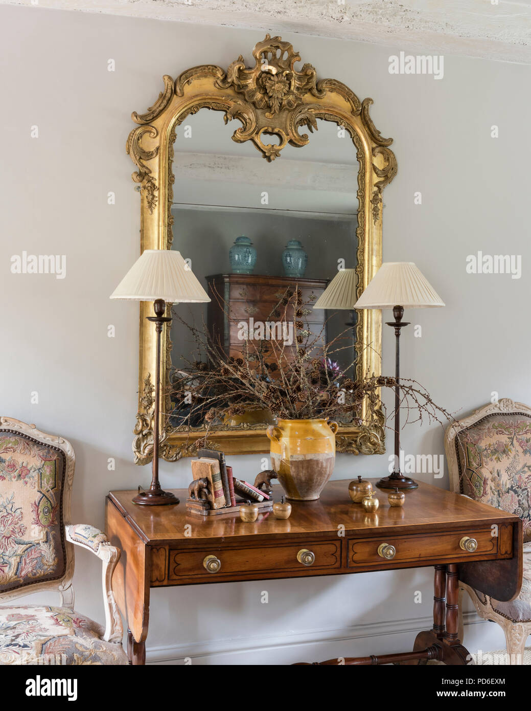 Gilt framed mirror above wooden console with pair of lamps and chairs ...
