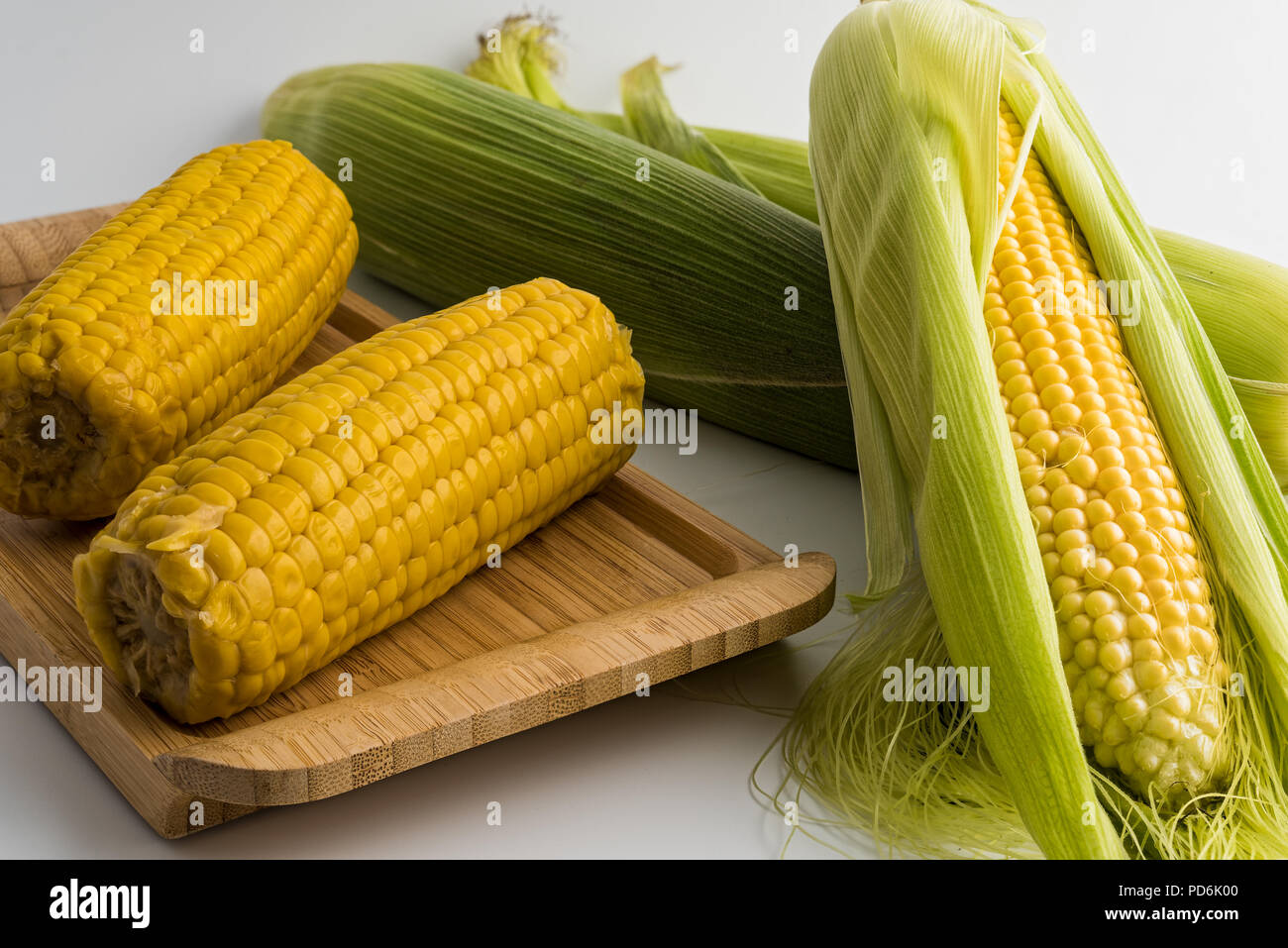 Boiled sweet corn and fresh corn on the cob with leaves on white ...