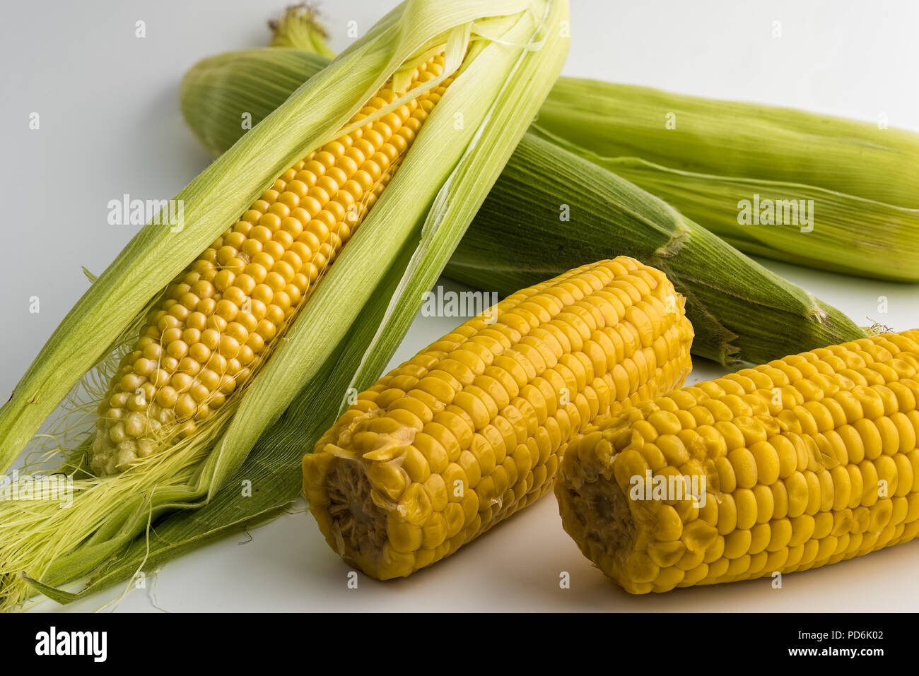 Boiled sweet corn and fresh corn on the cob with leaves on white ...