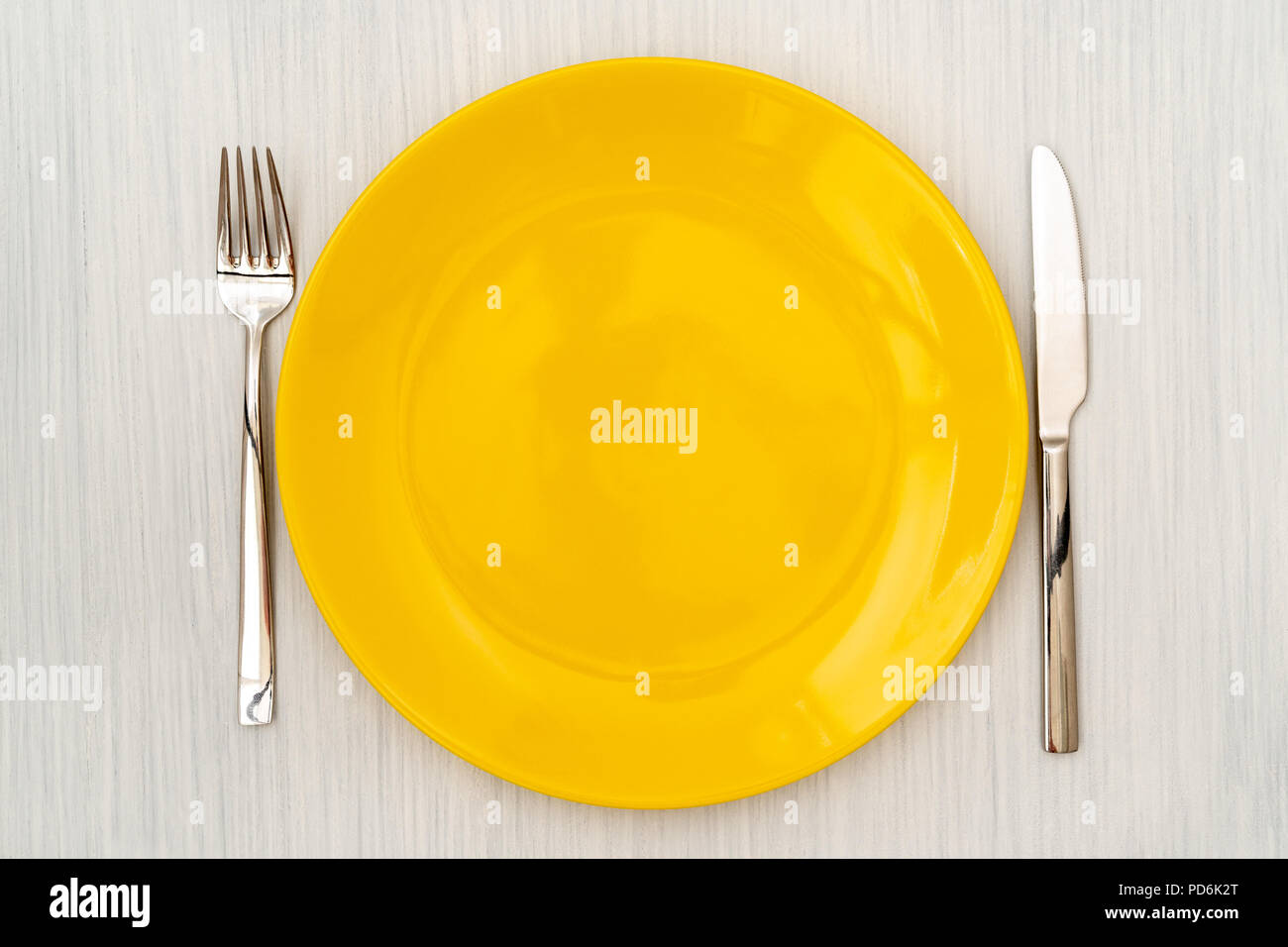 Empty yellow plate with fork and knife. View from above Stock Photo - Alamy
