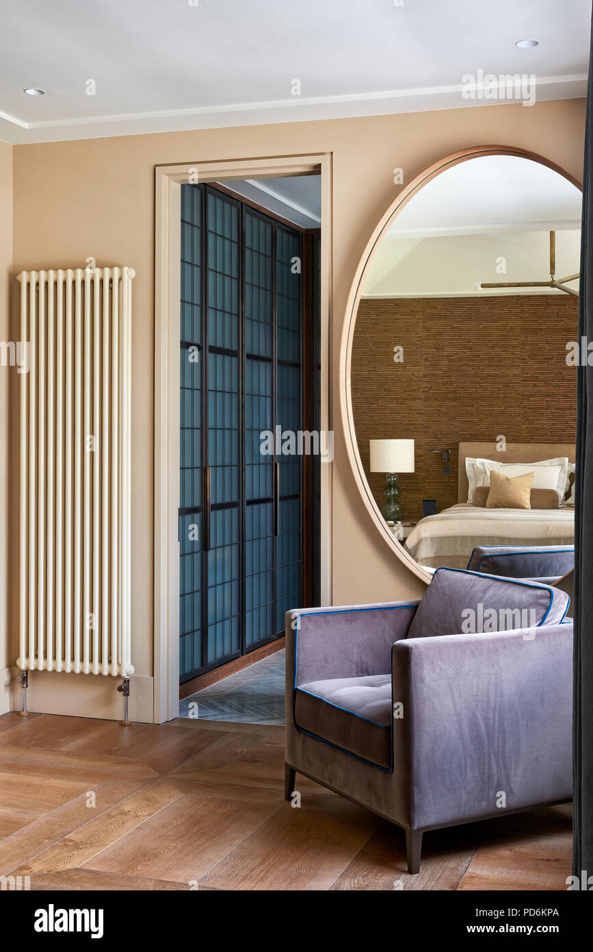 Oversized circular mirror and radiator with vintage chair at doorway ...