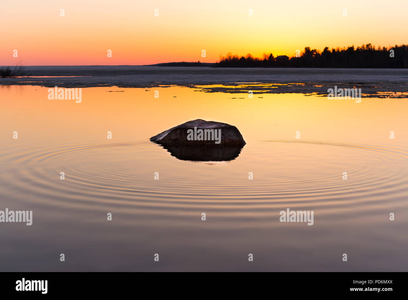Rock in the water with ripples around it and colourful sunset ...