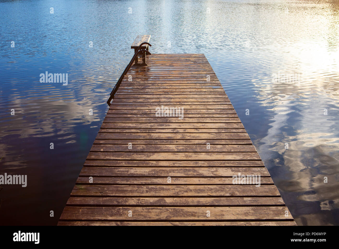 Beautiful wooden pier with clouds and sun reflected on calm and blue ...