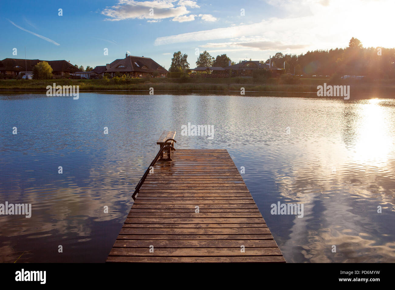 Beautiful wooden pier with clouds and sun reflected on calm and blue ...