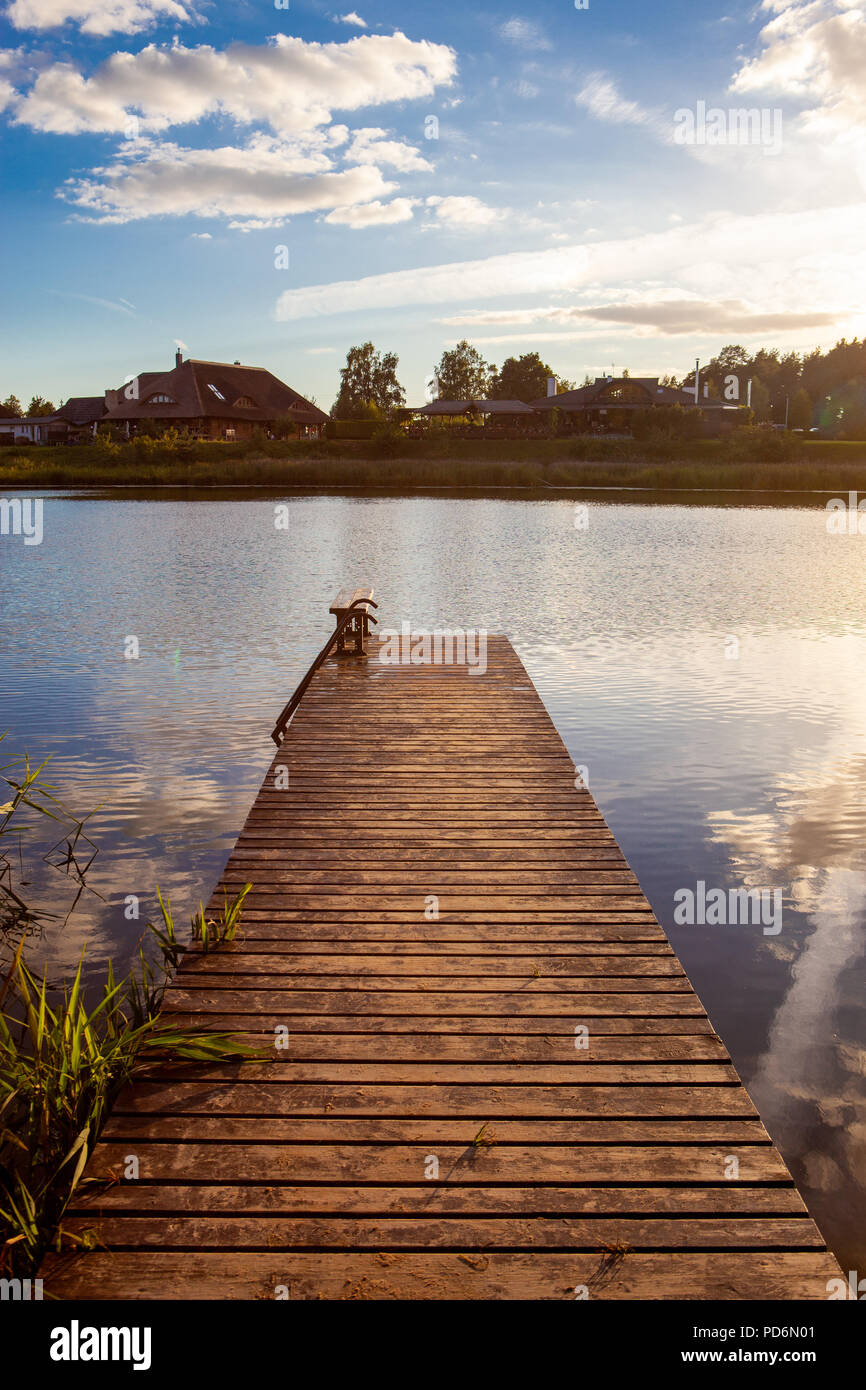 Beautiful wooden pier with clouds and sun reflected on calm and blue ...