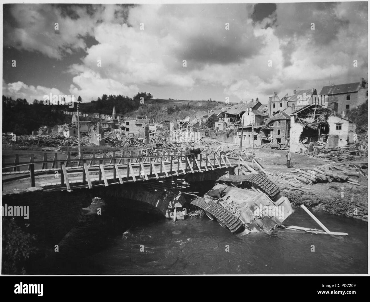 An overturned German tank lies in a shallow stream alongside a rebuilt ...