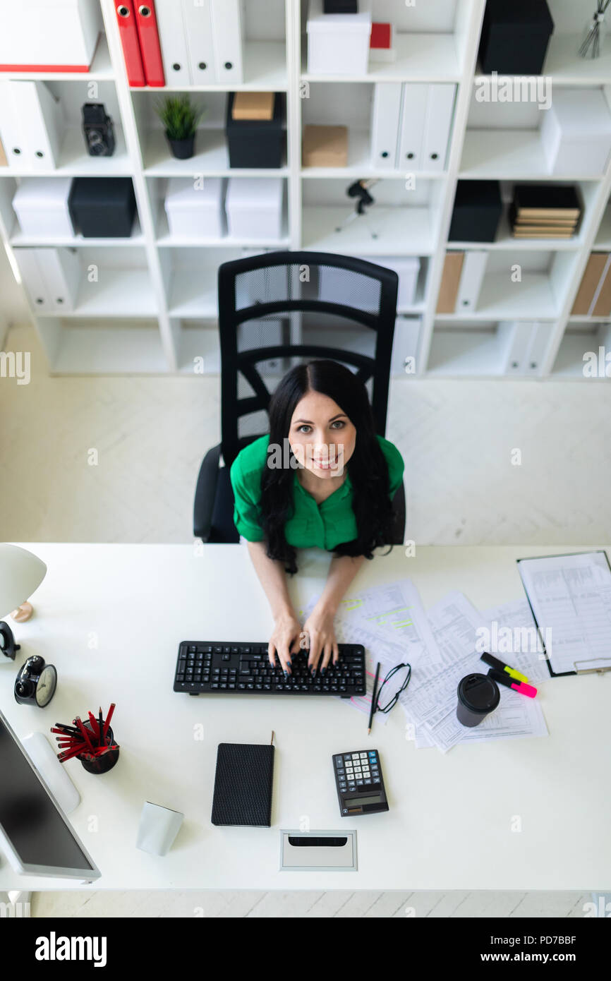 Top view of a young girl sitting at an office desk and typing on a ...