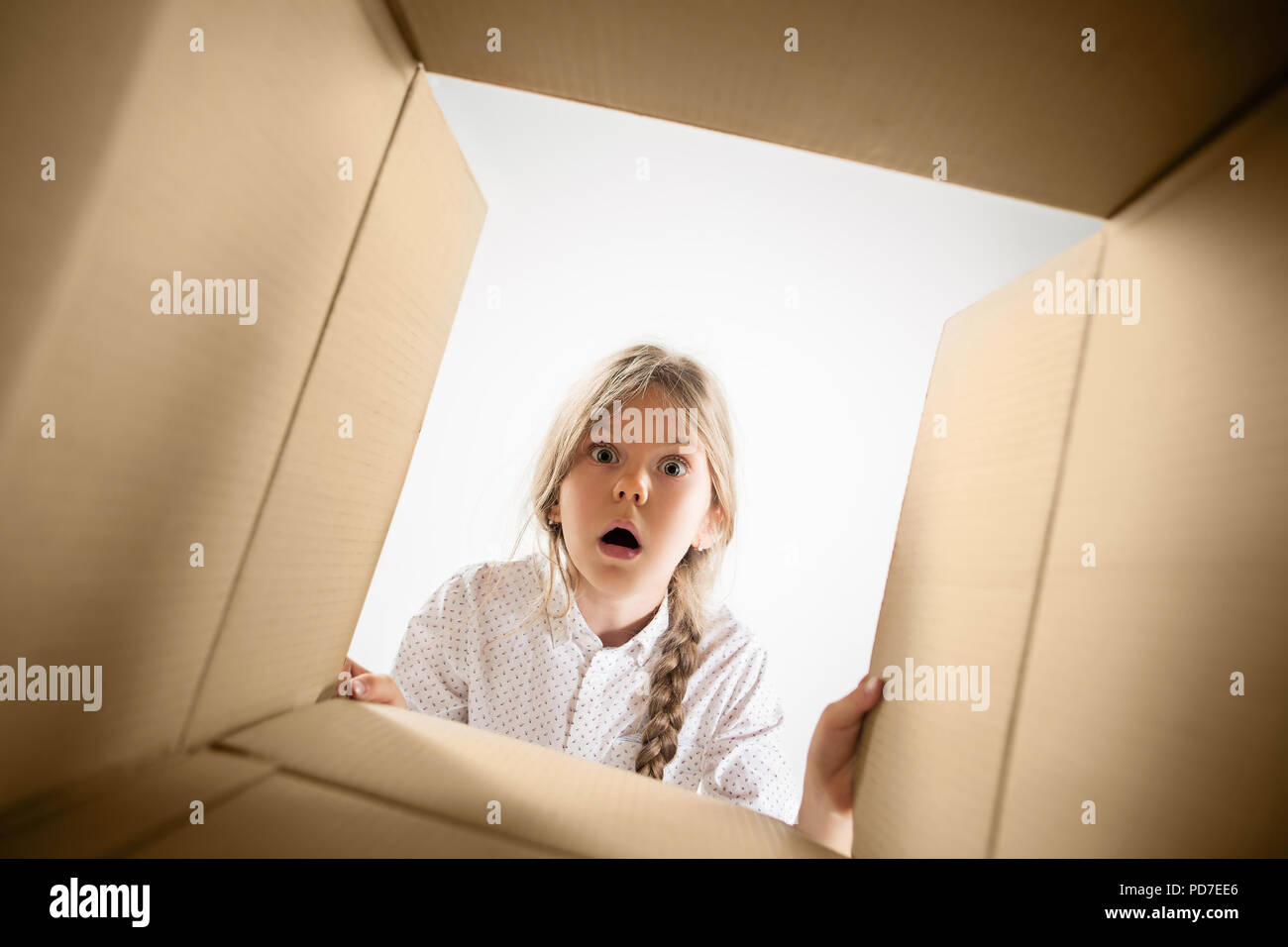The surprised girl unpacking, opening carton box and looking inside ...
