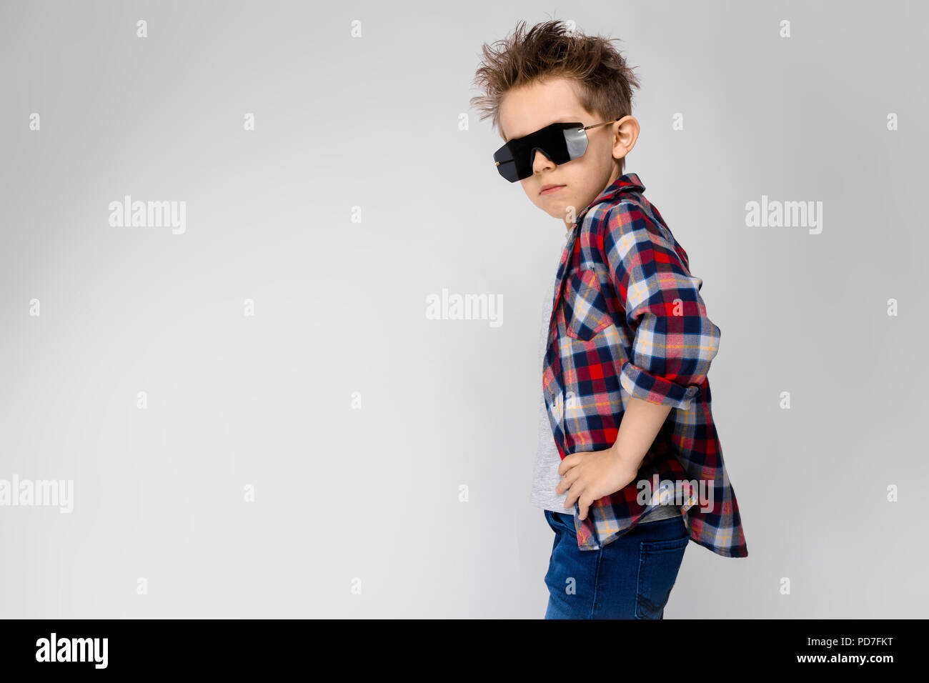 A handsome boy in a plaid shirt, gray shirt and jeans stands on a gray ...