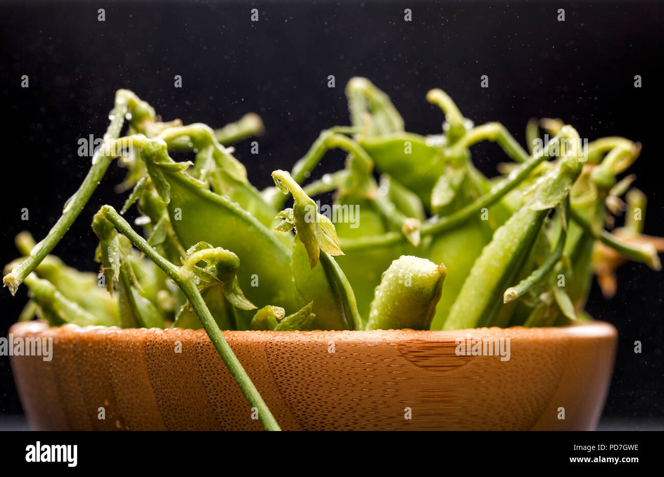 Photo of green pea pods in wooden cup on blank black background in ...