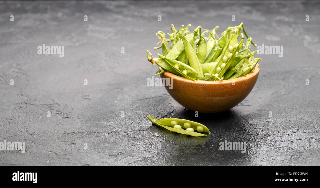 Photo of green pea pods in wooden plate on blank black table with pod ...
