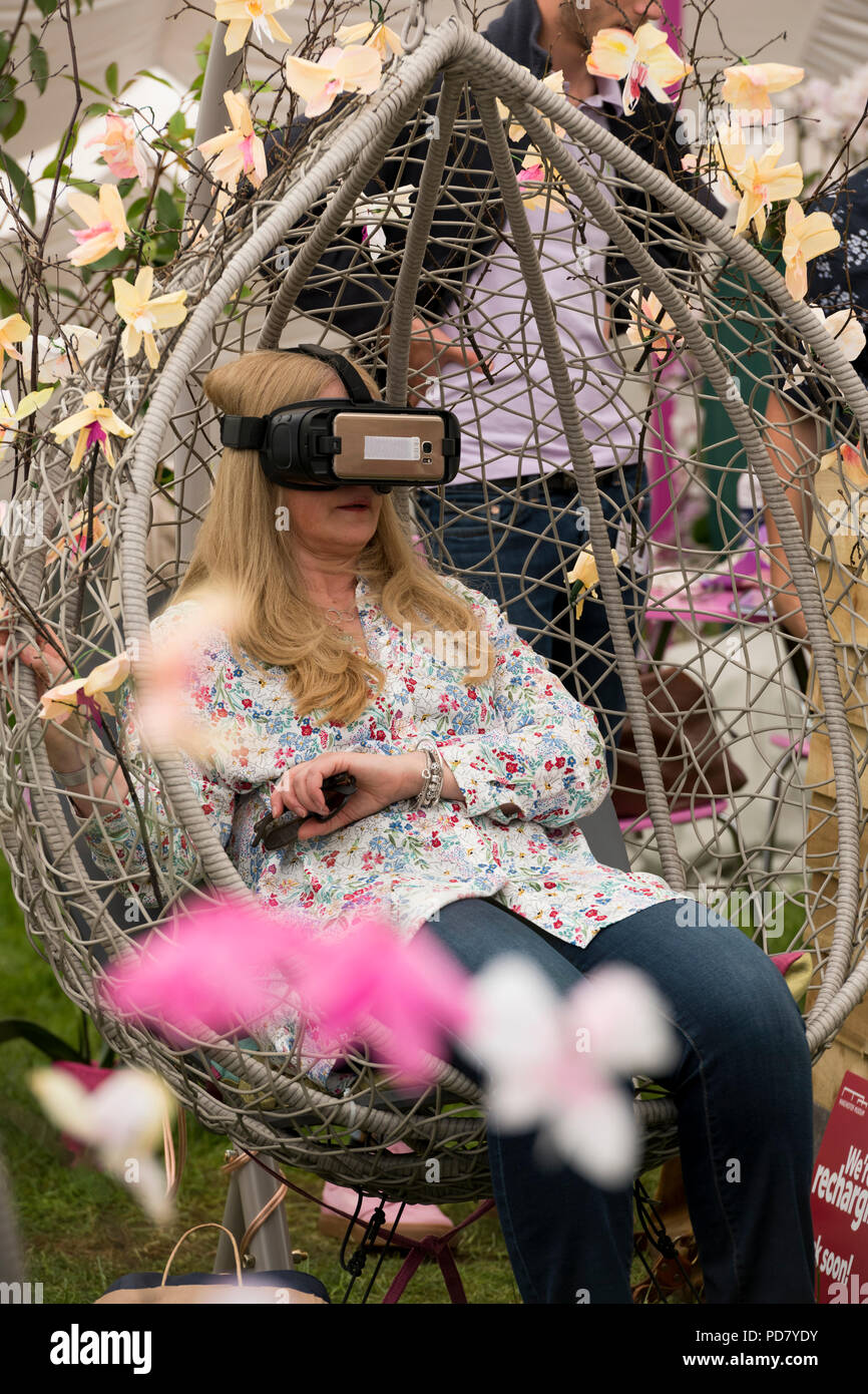 Woman wearing VR headset, sitting in seat among flowers at virtual ...
