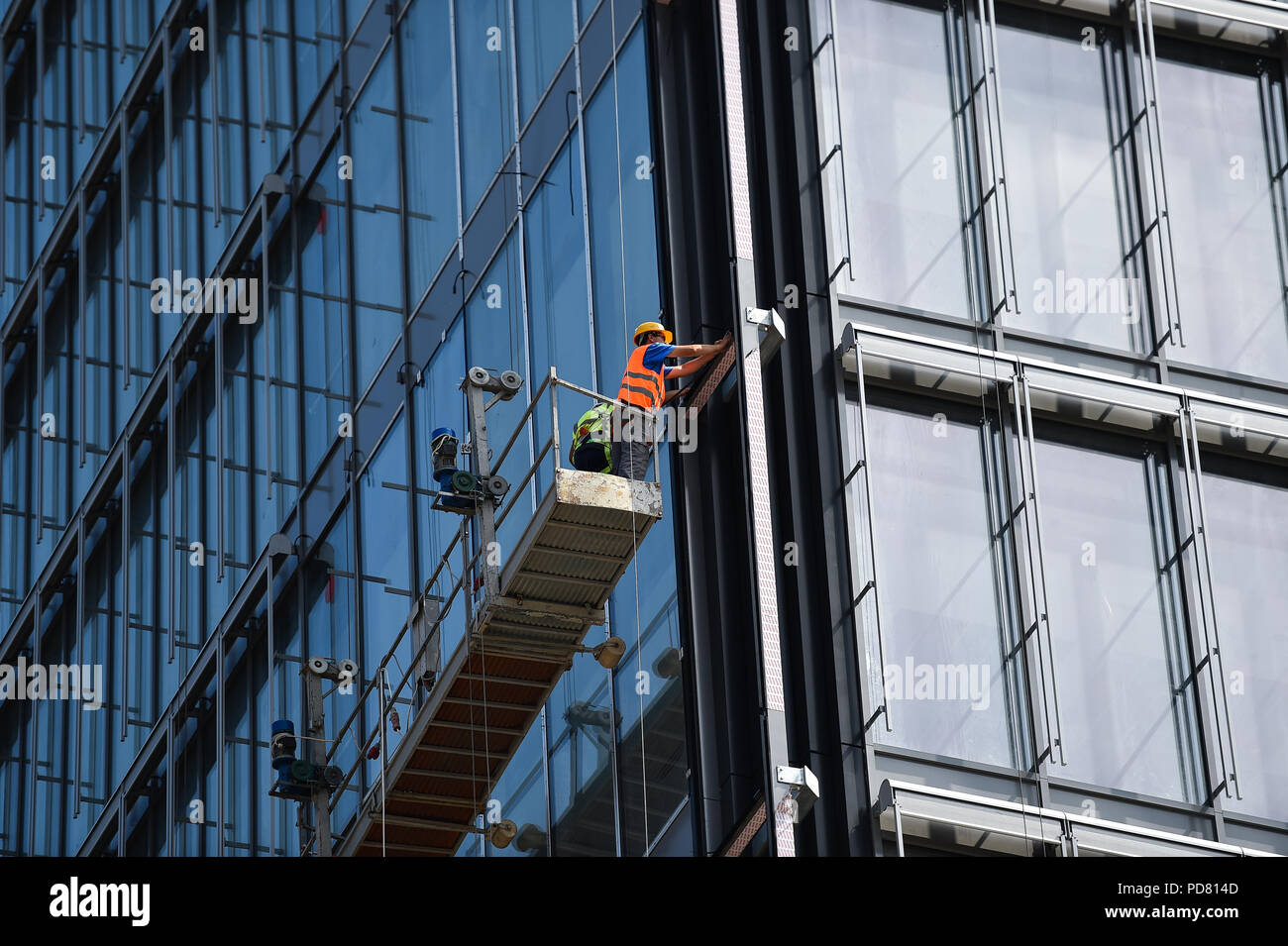 Construction workers on a suspended platform on a skyscraper glass ...