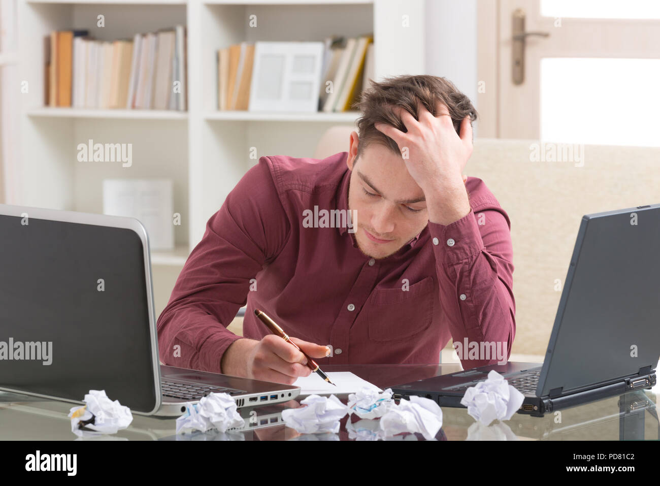 Overworked young man sitting at the desk and holding his head Stock ...